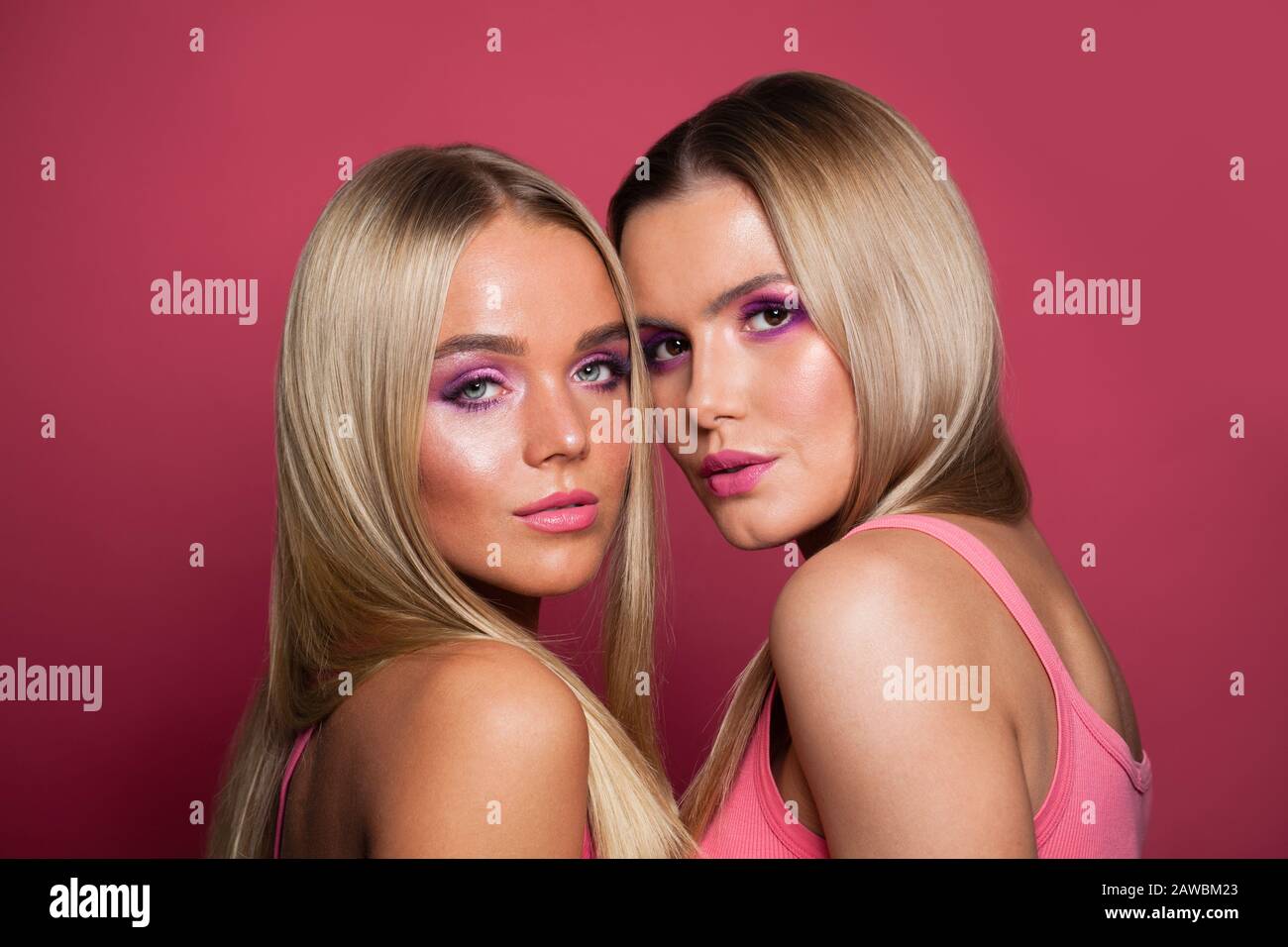 Two blonde models with long straight hair and makeup on pink background ...