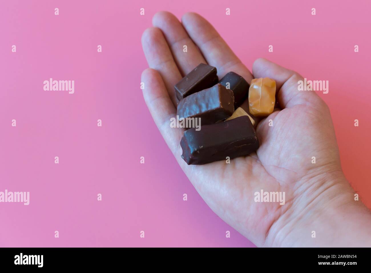 Hand with chocolates on a pink background. Enjoying sweets. Sweet ...