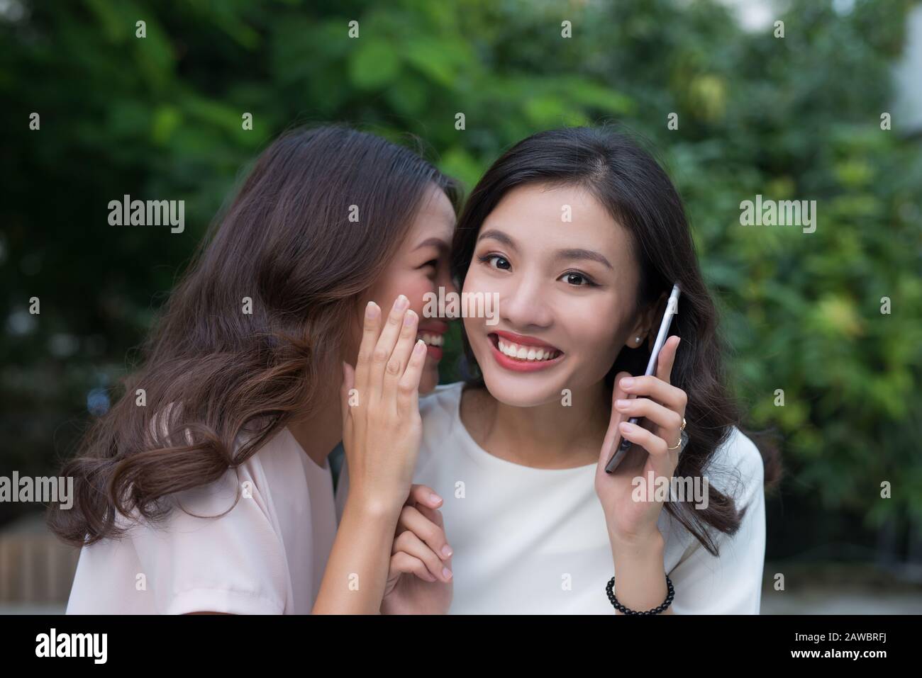 Two beautiful smiling girls sharing a secret in the park Stock Photo ...