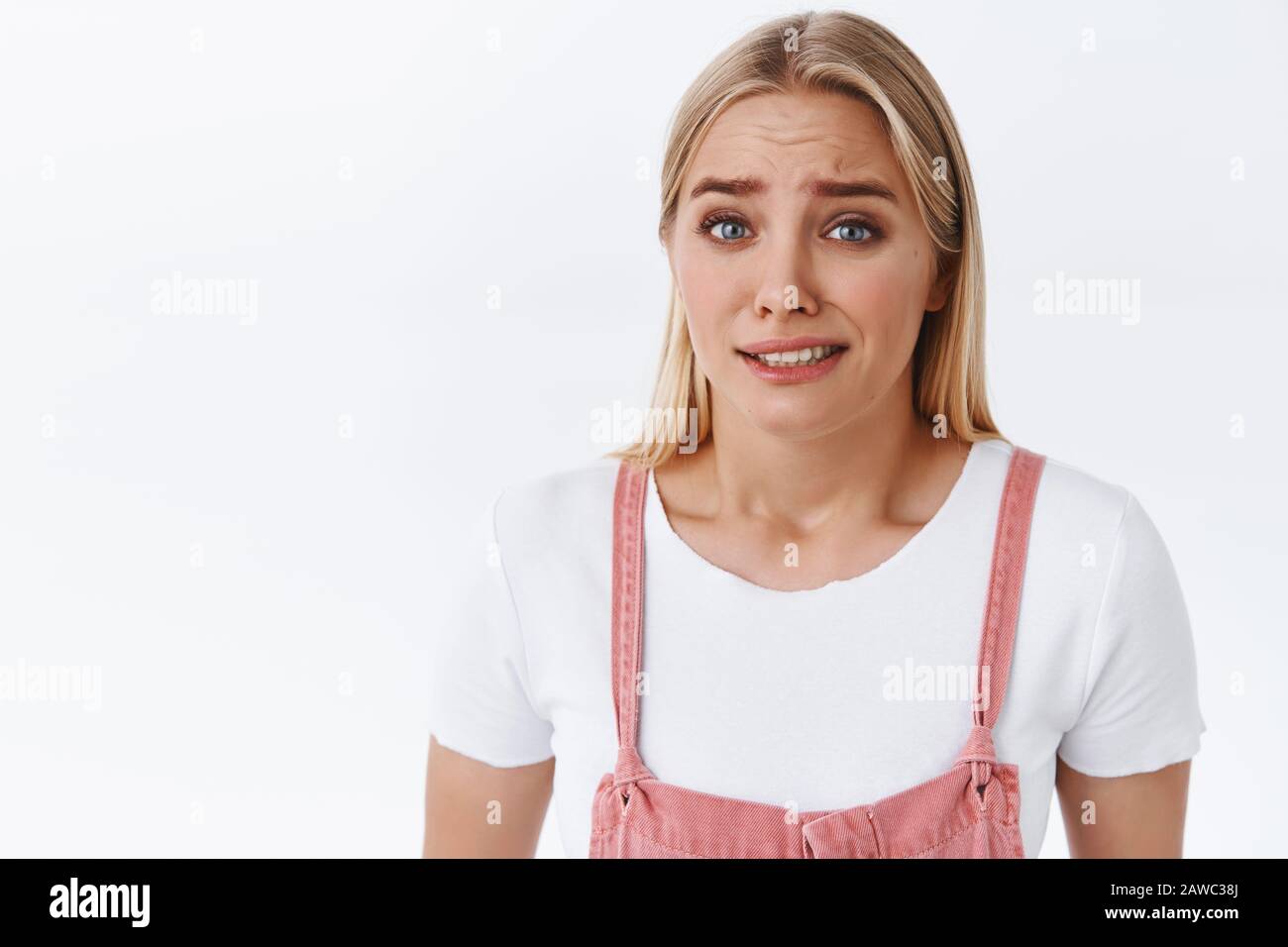 Anxious and embarrassed blond young woman with blue eyes, frowning and ...