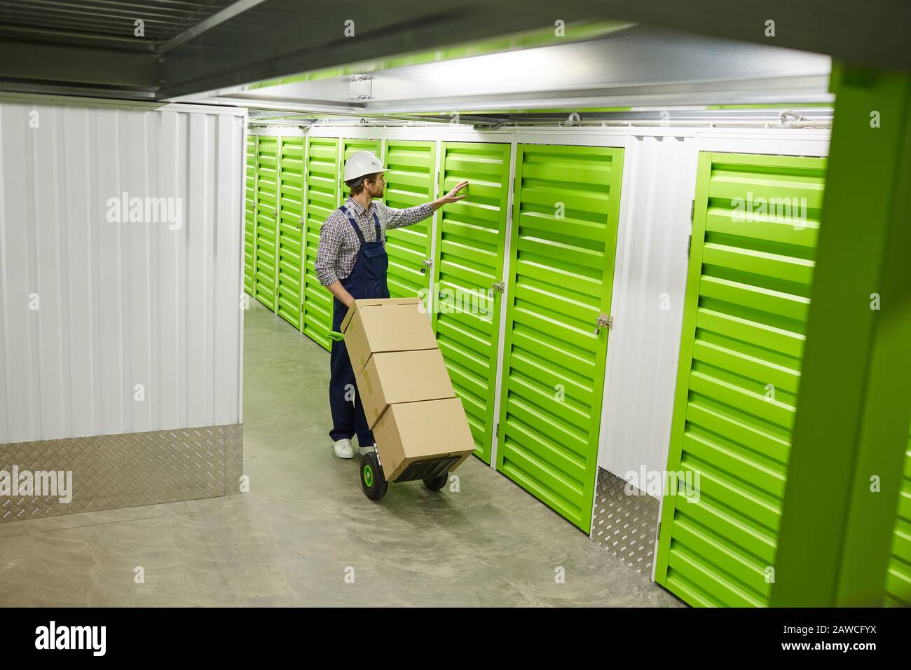 Worker in working clothing standing with cart full of boxes and opening ...