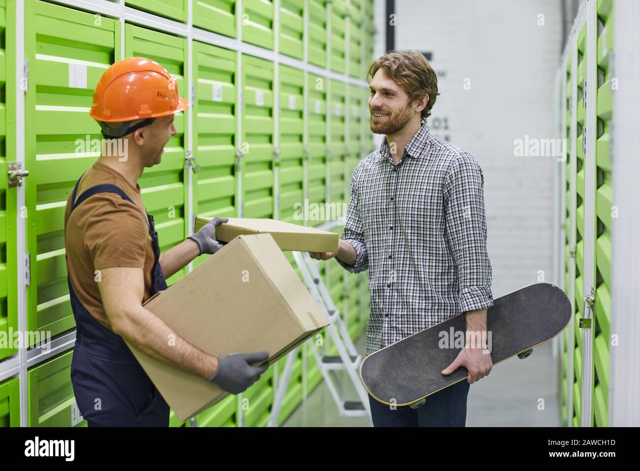 Young worker in work helmet giving a parcel to young man while they ...