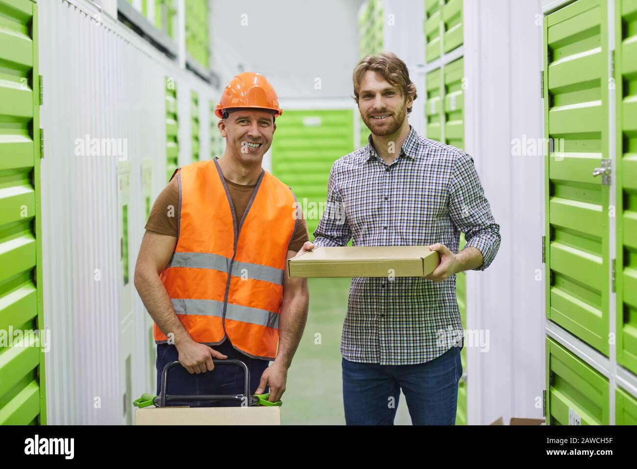 Portrait of two young workers with cardboard boxes smiling at camera ...