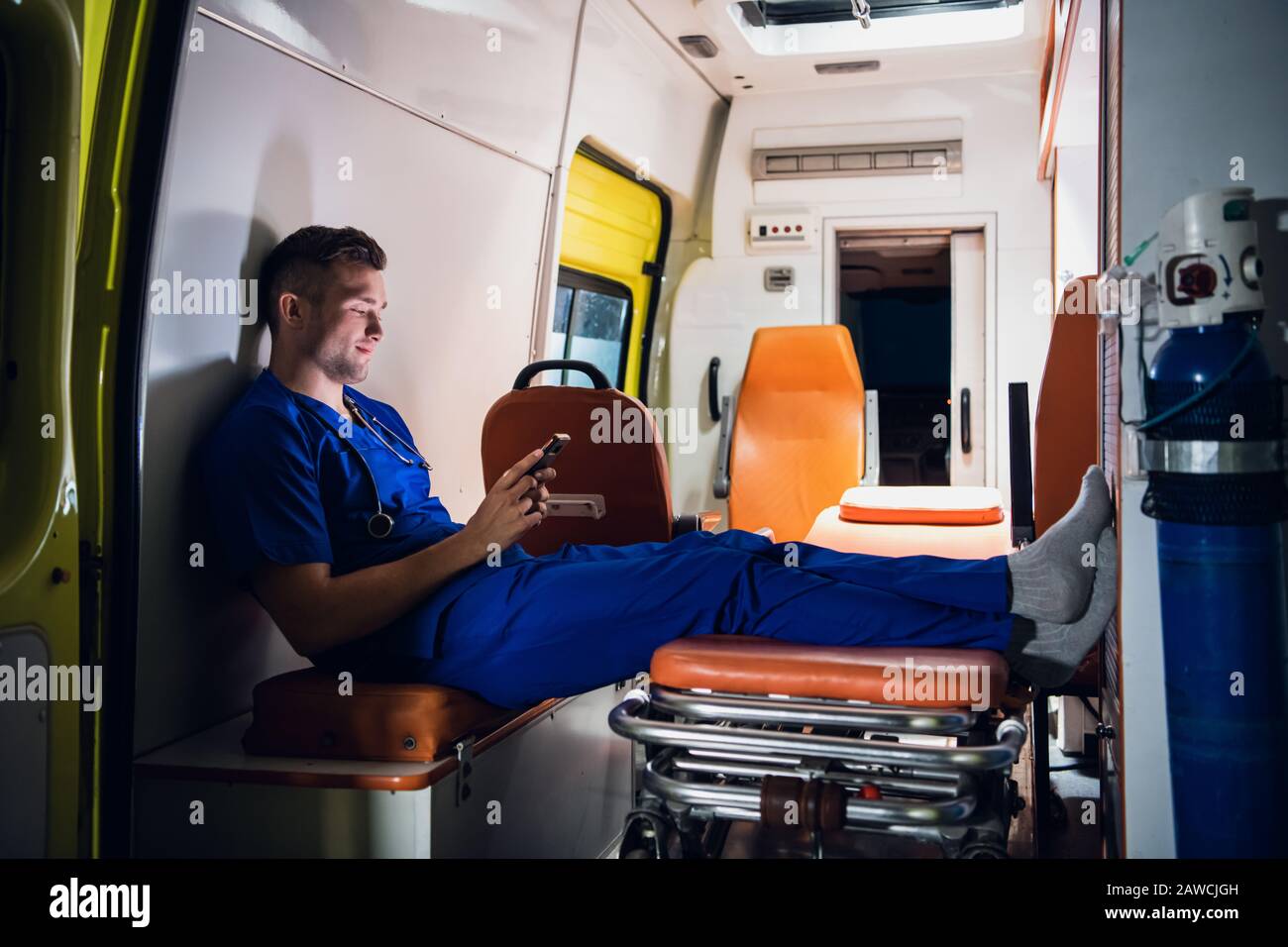 Young paramedic in blue medical uniform sits with phone in his hands in ...