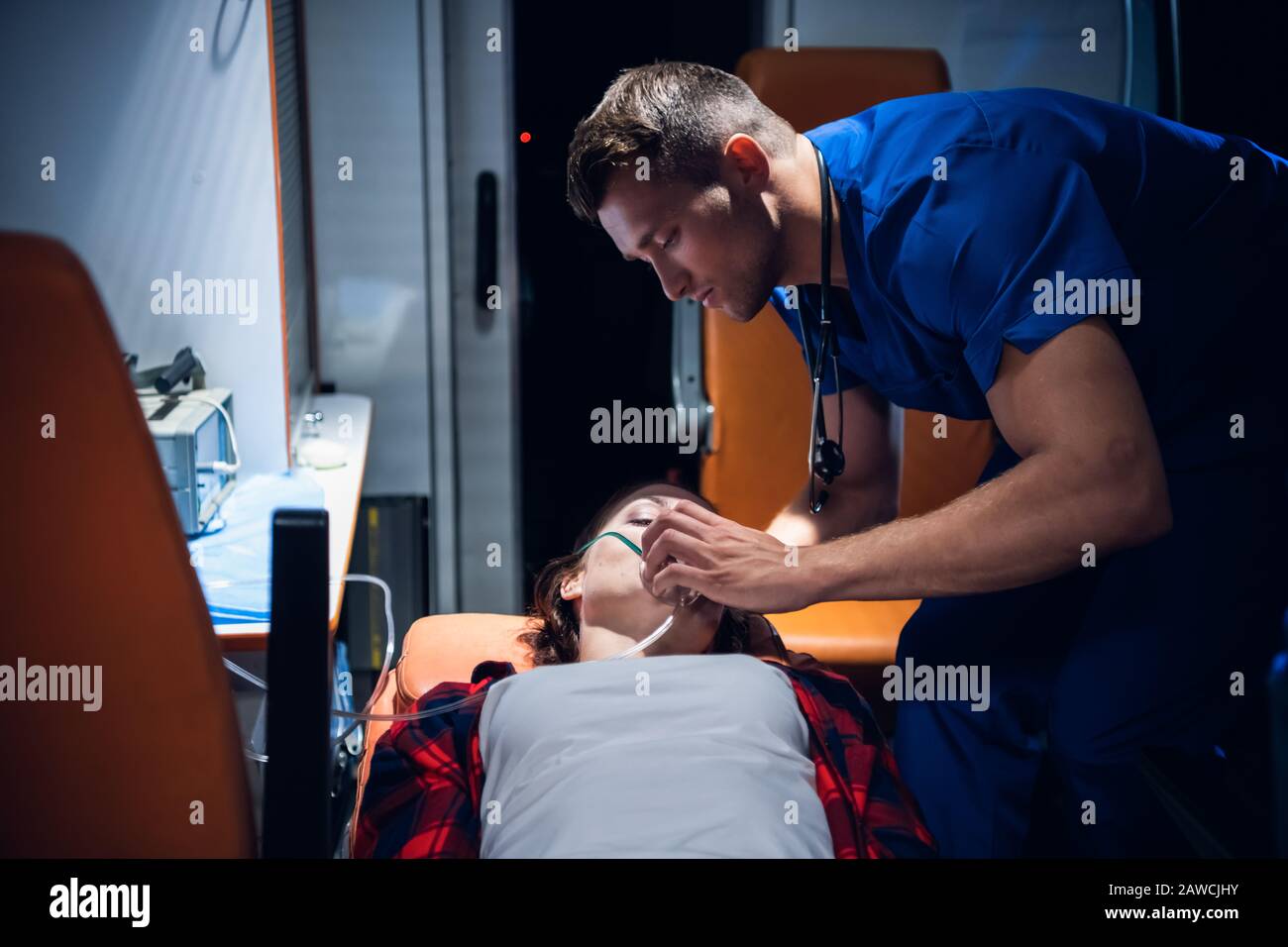 Young corpsman in medical uniform puts mask on woman liyng on stretcher ...