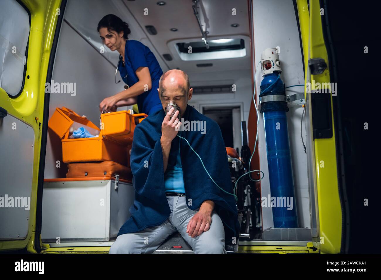 Man in blanket breathe through oxygen mask, young nurse in uniform ...