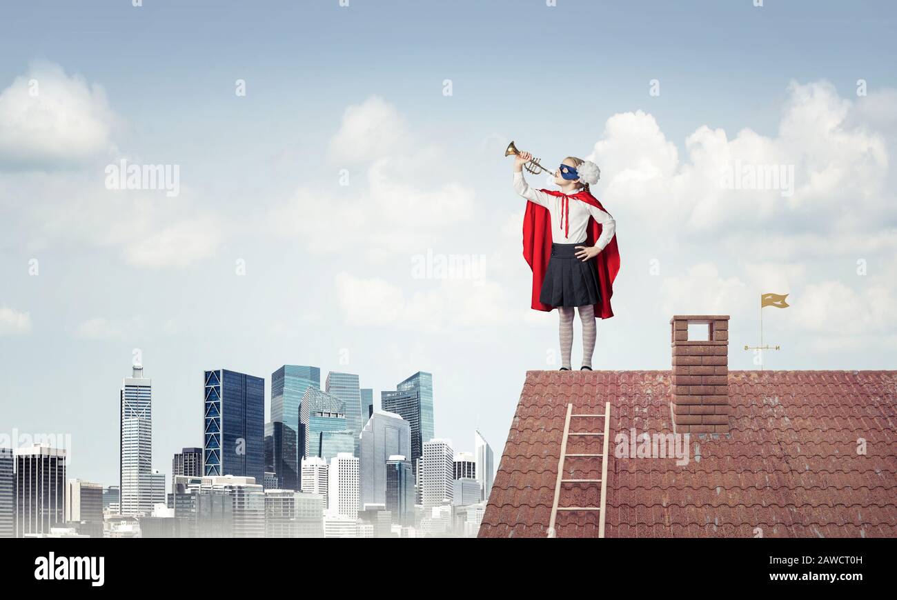 Girl power concept with kid wearing cape and mask and playing trumpet ...