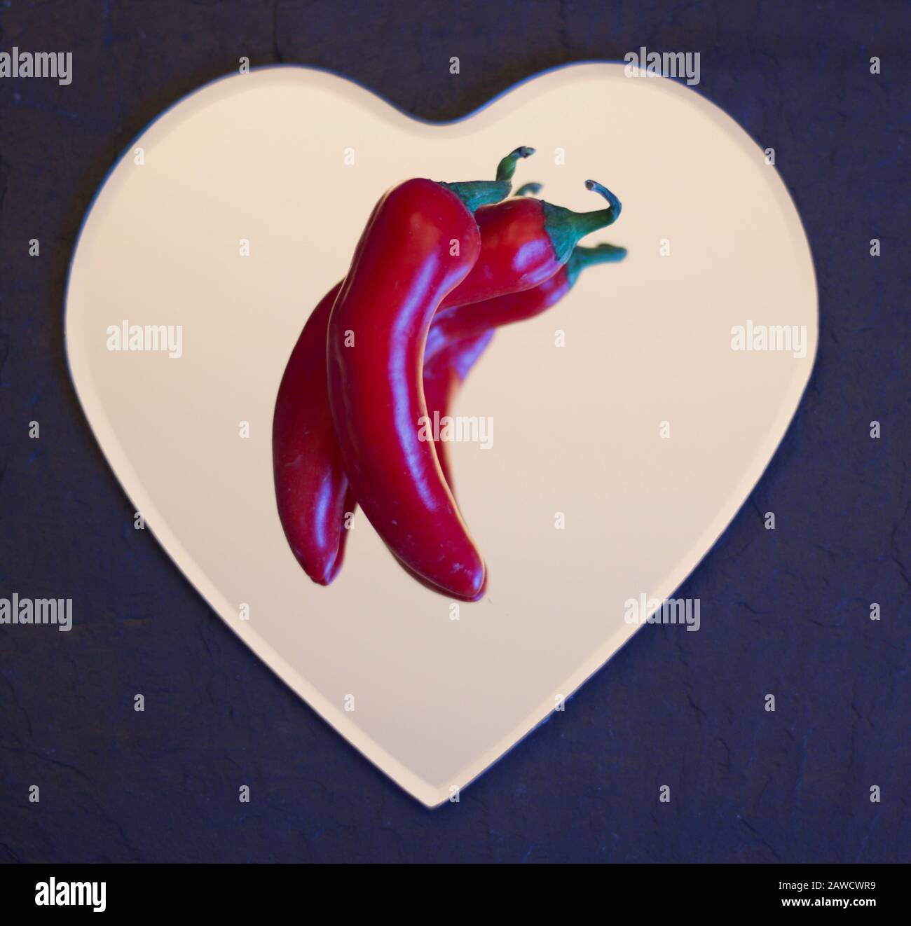 Two red chilli peppers lying on heart background Stock Photo - Alamy