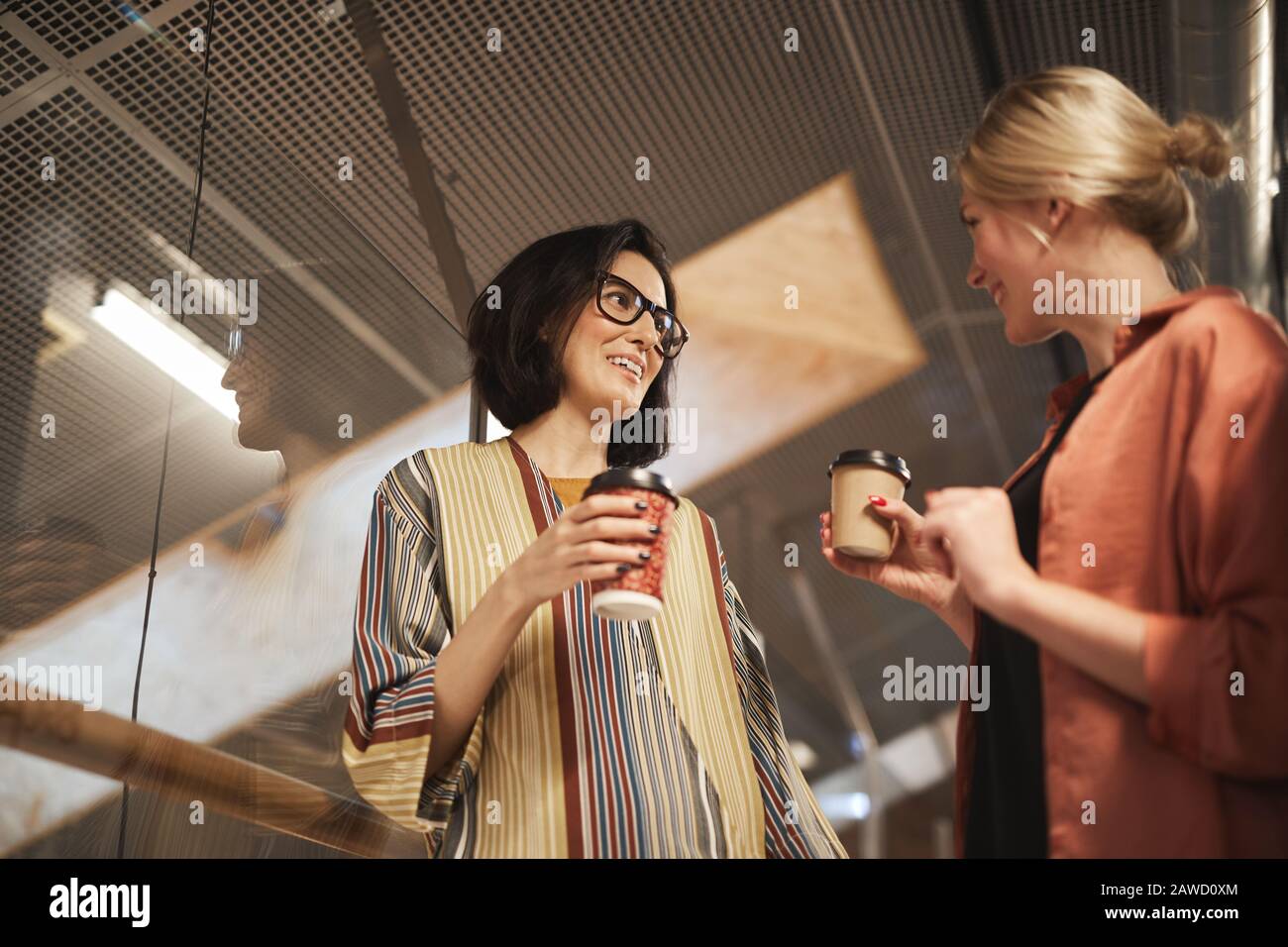 Two business colleagues holding cups of coffee and talking to each ...