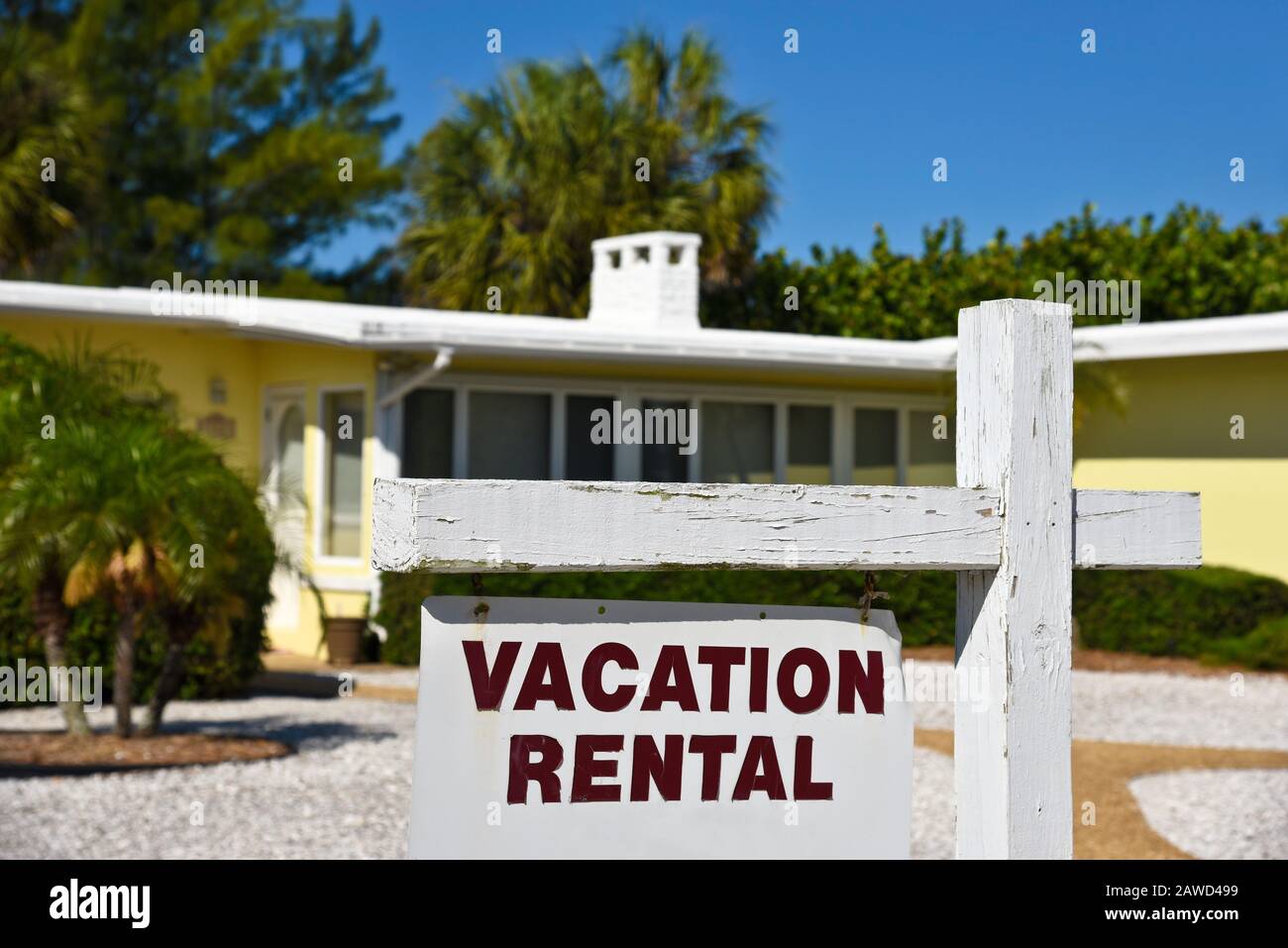 A Vacation Rental Sign in front of a yellow one story home on the beach ...