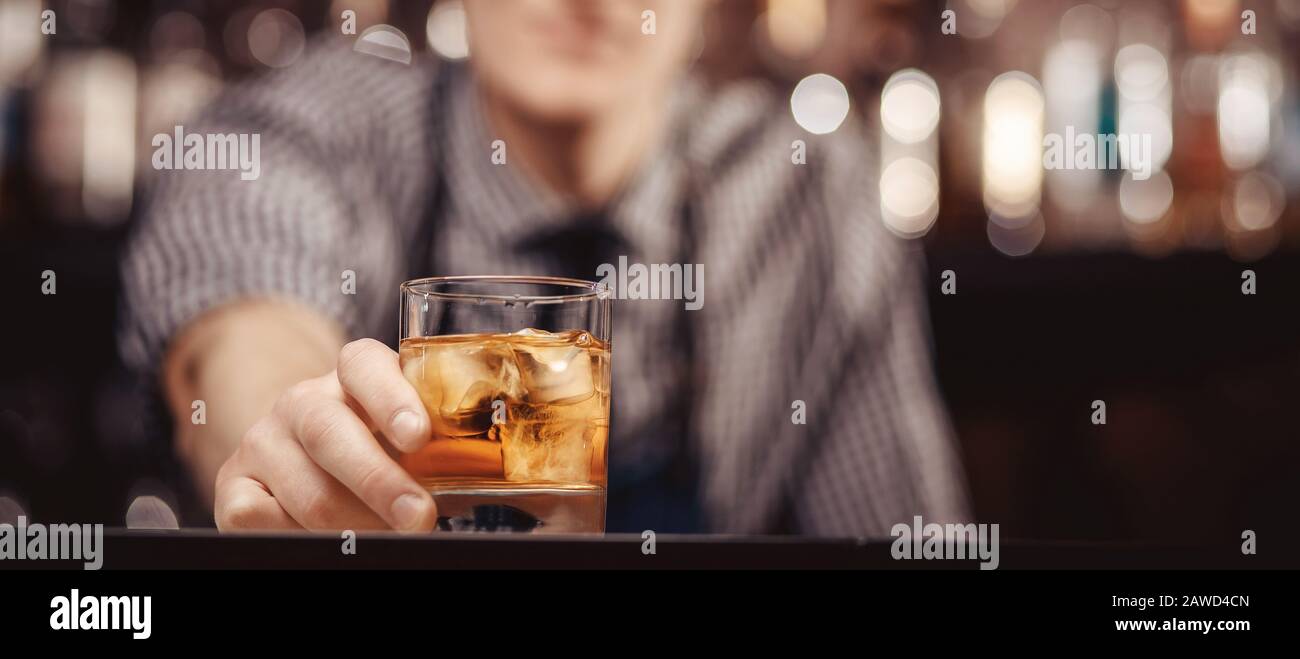 Barman holds out glass of whiskey with ice to male visitor. Concept ...