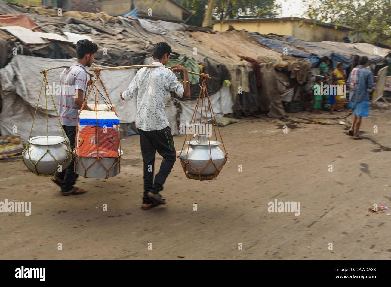 Indian men carry food and drinks in pots on yoke along the street ...