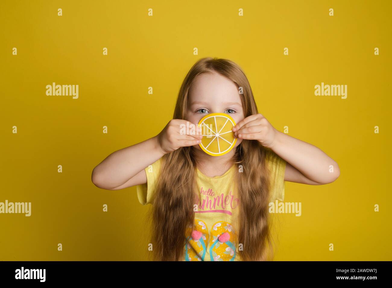 Portrait of smiling little girl holding slice of lemon near eye looking ...