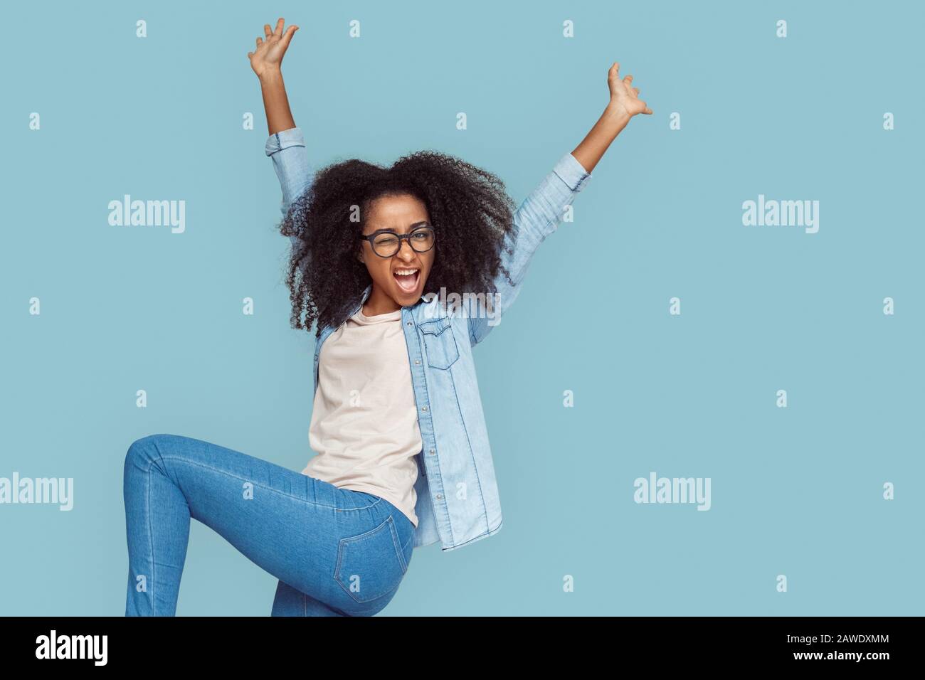 Freestyle. African girl in glasses standing isolated on gray leg up ...