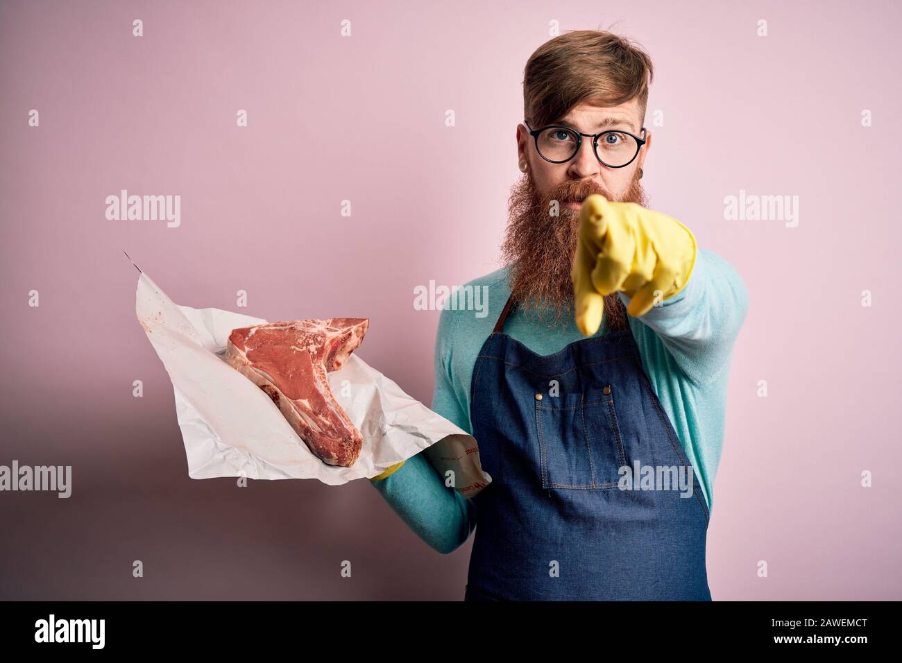 Redhead Irish butcher man with beard holding raw beef steak over pink ...