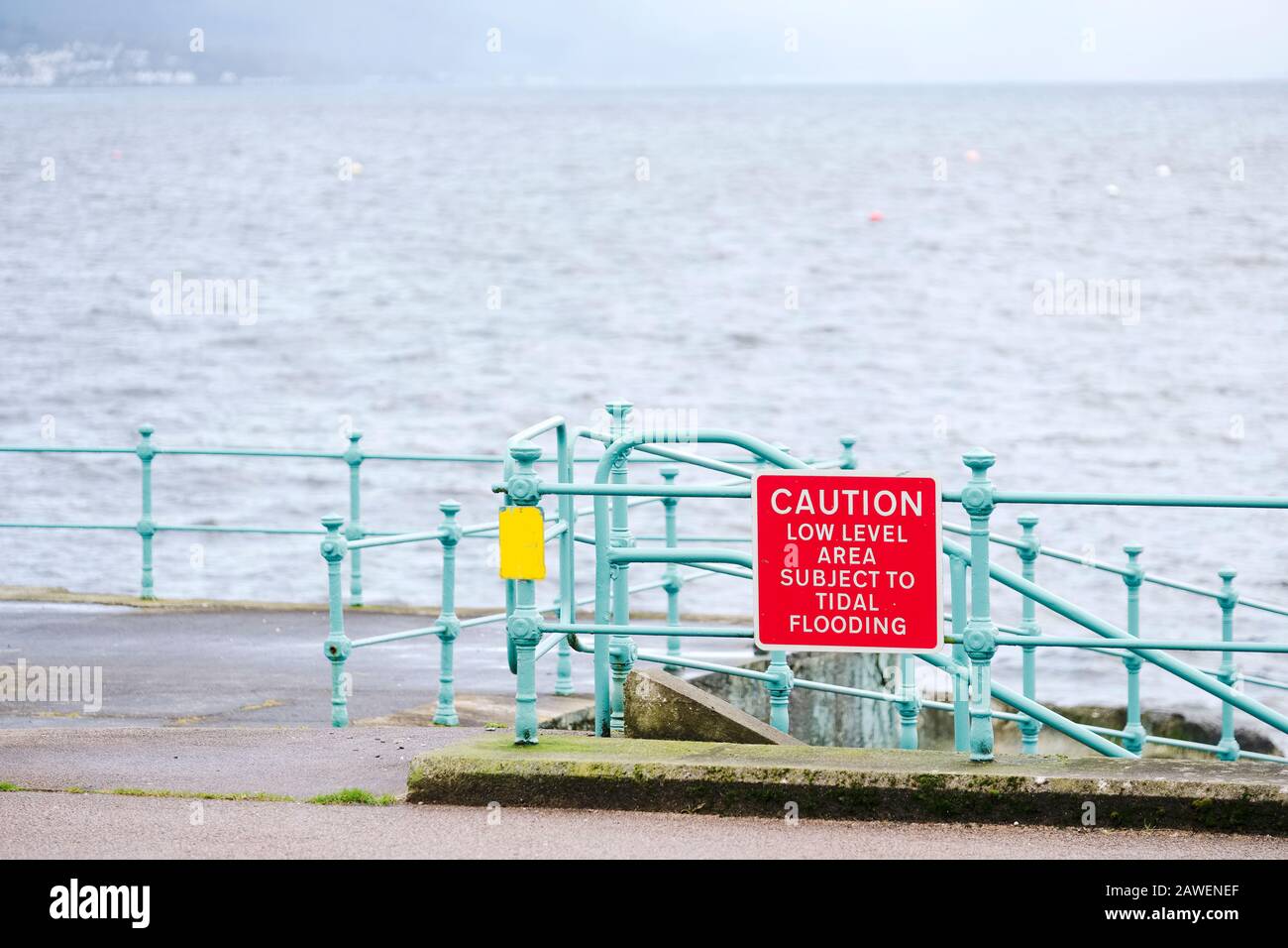 Low tide area subject to tidal flooding warning sign at harbour wall ...