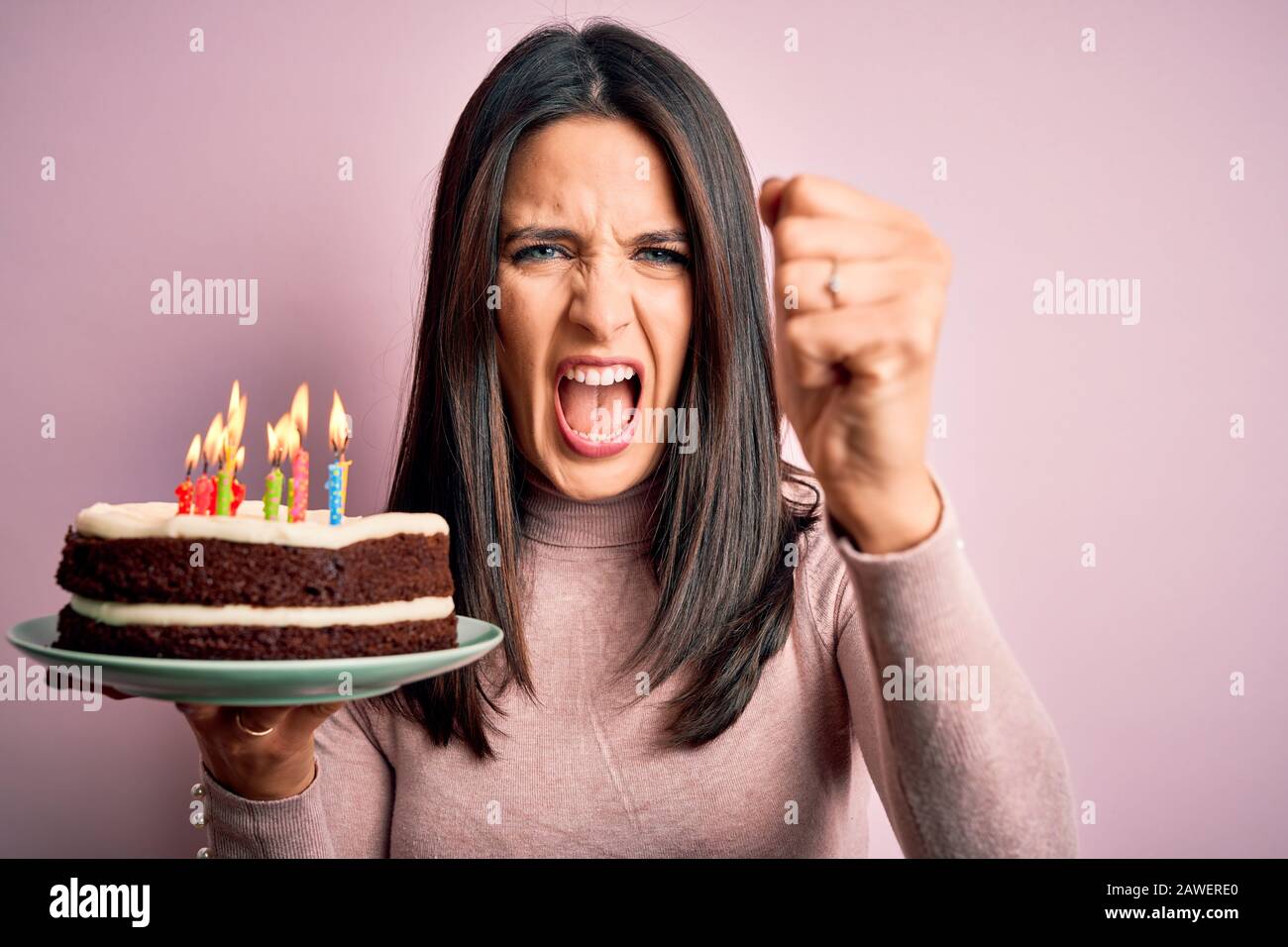 Young woman with blue eyes holding birthday cake with candles over pink ...