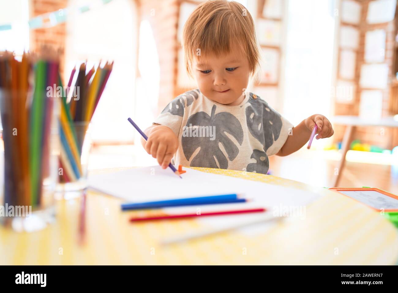 Adorable toddler drawing using paper and pencil around lots of toys at ...