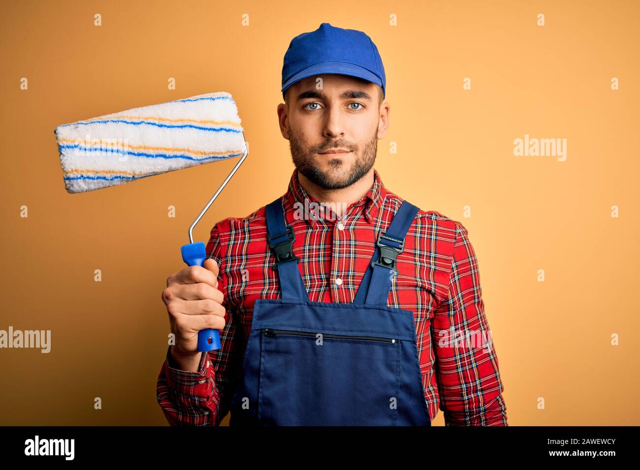 Young handsome painter man painting wall using roller over isolated ...