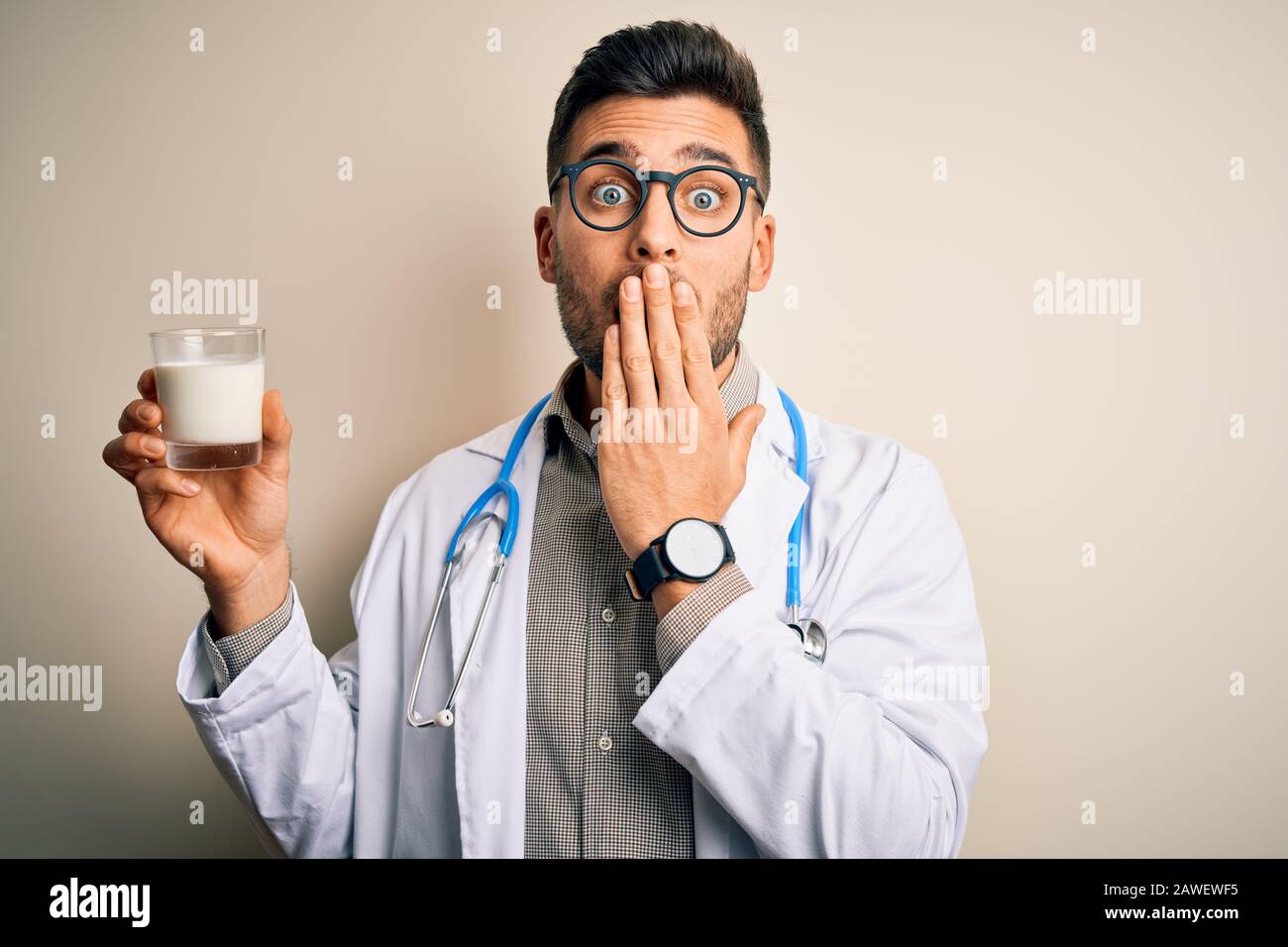 Young doctor man wearing stethoscope holding a glass of milk over ...
