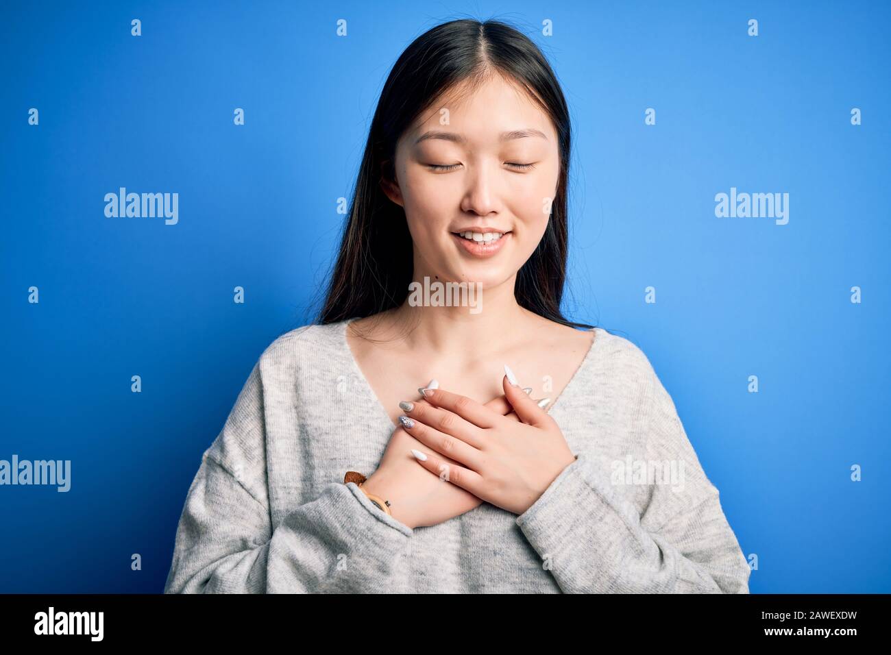 Young beautiful asian woman wearing casual sweater standing over blue ...