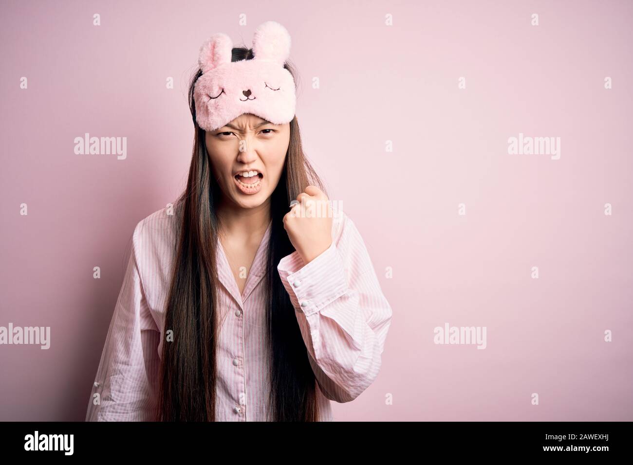 Young asian woman wearing pajama and sleep mask over pink isolated ...