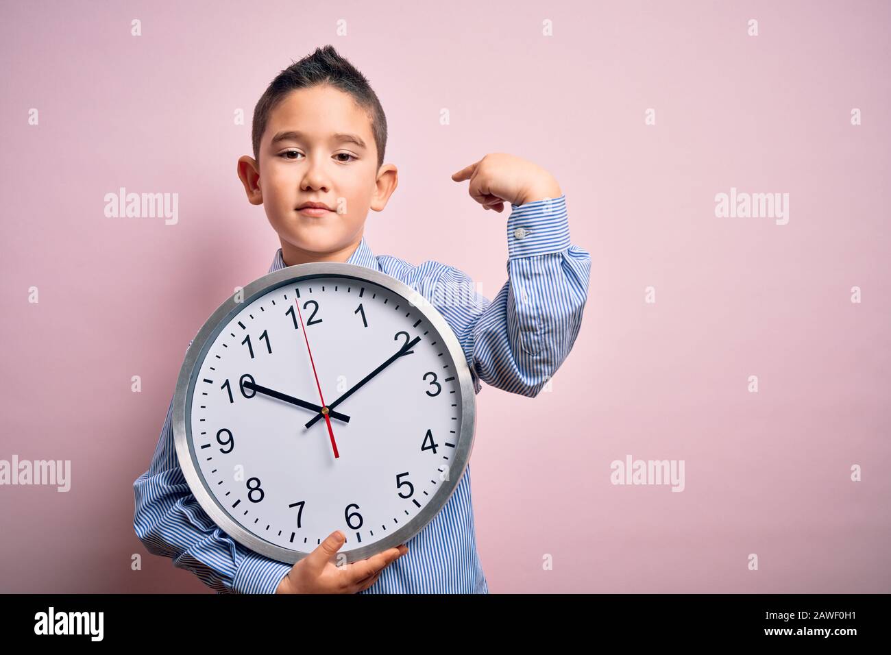 Young little boy kid holding big minute clock over isolated pink ...