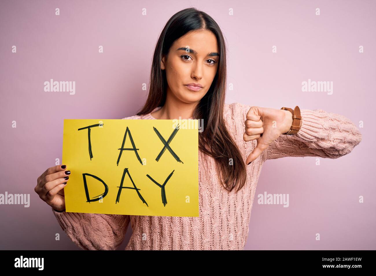 Young beautiful brunette woman holding paper with tax day message over ...