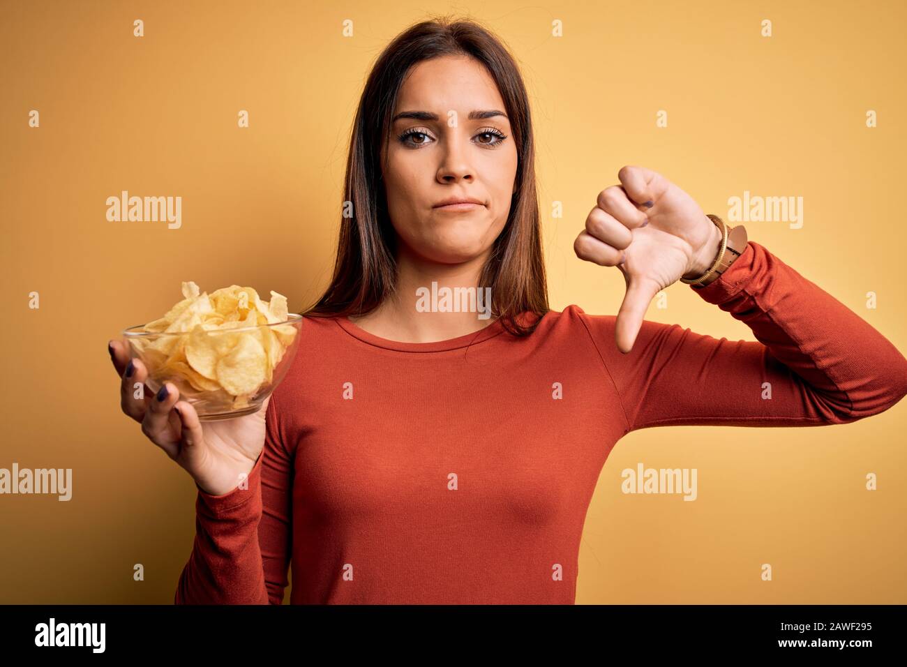 Young beautiful brunette woman holding bowl with chips potatoes over ...