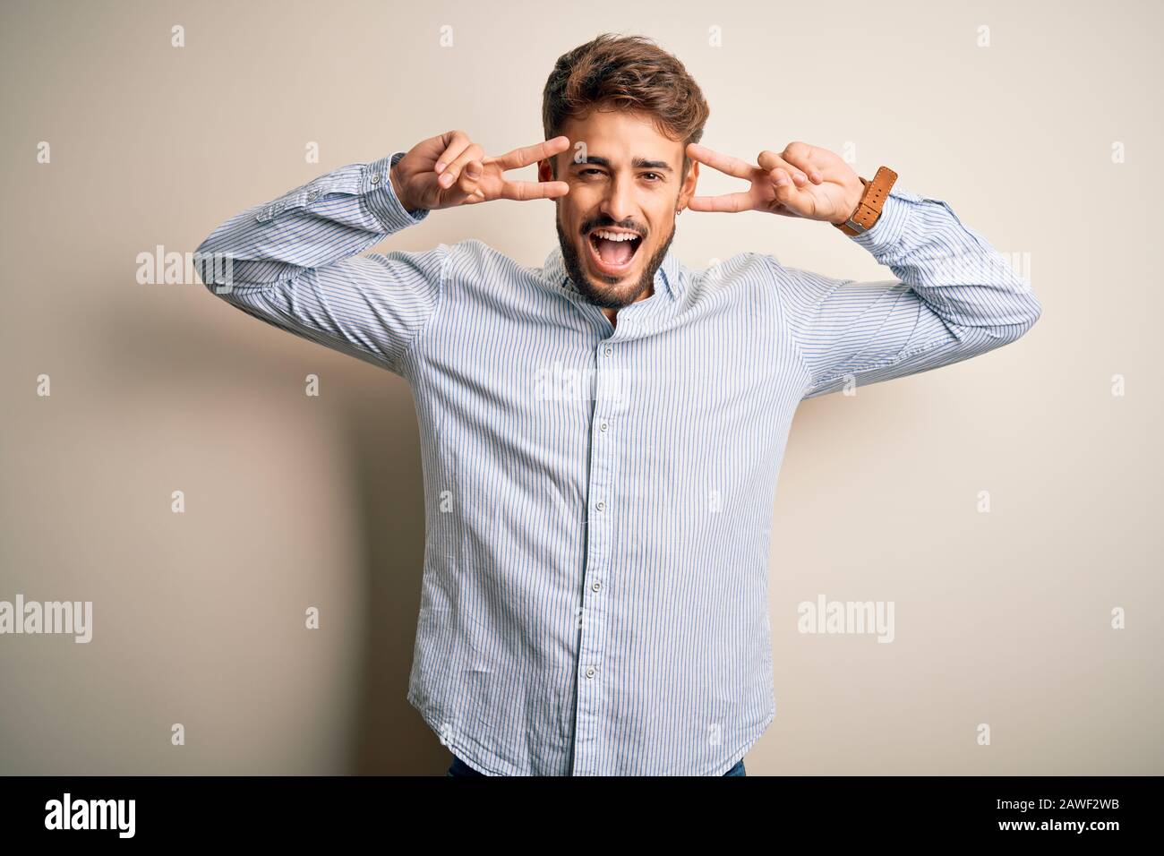 Young handsome man with beard wearing striped shirt standing over white ...