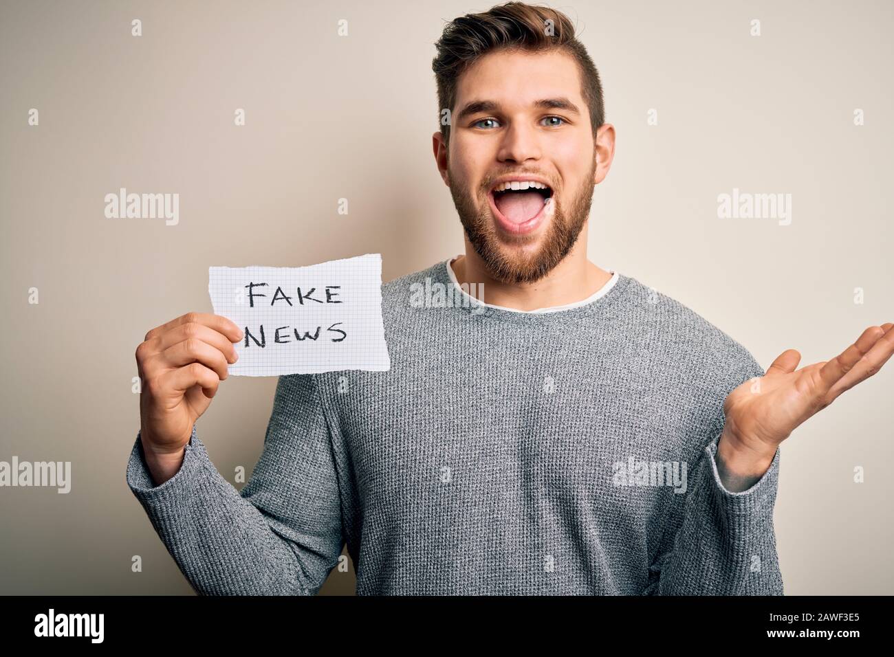 Young blond man with beard and blue eyes holding paper with fake news ...