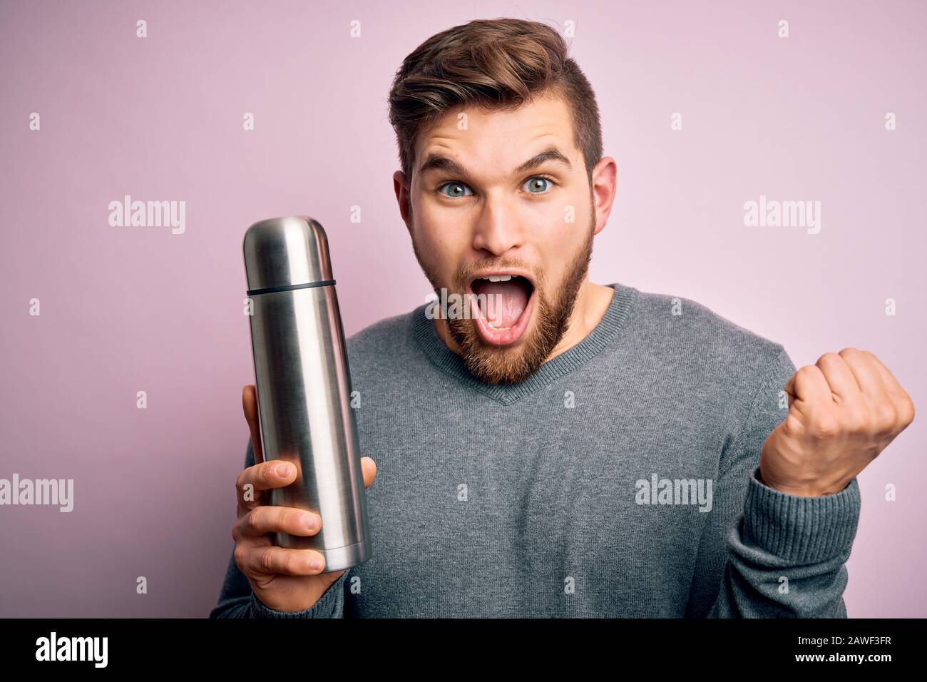 Young blond man with beard and blue eyes holding thermo with water over ...
