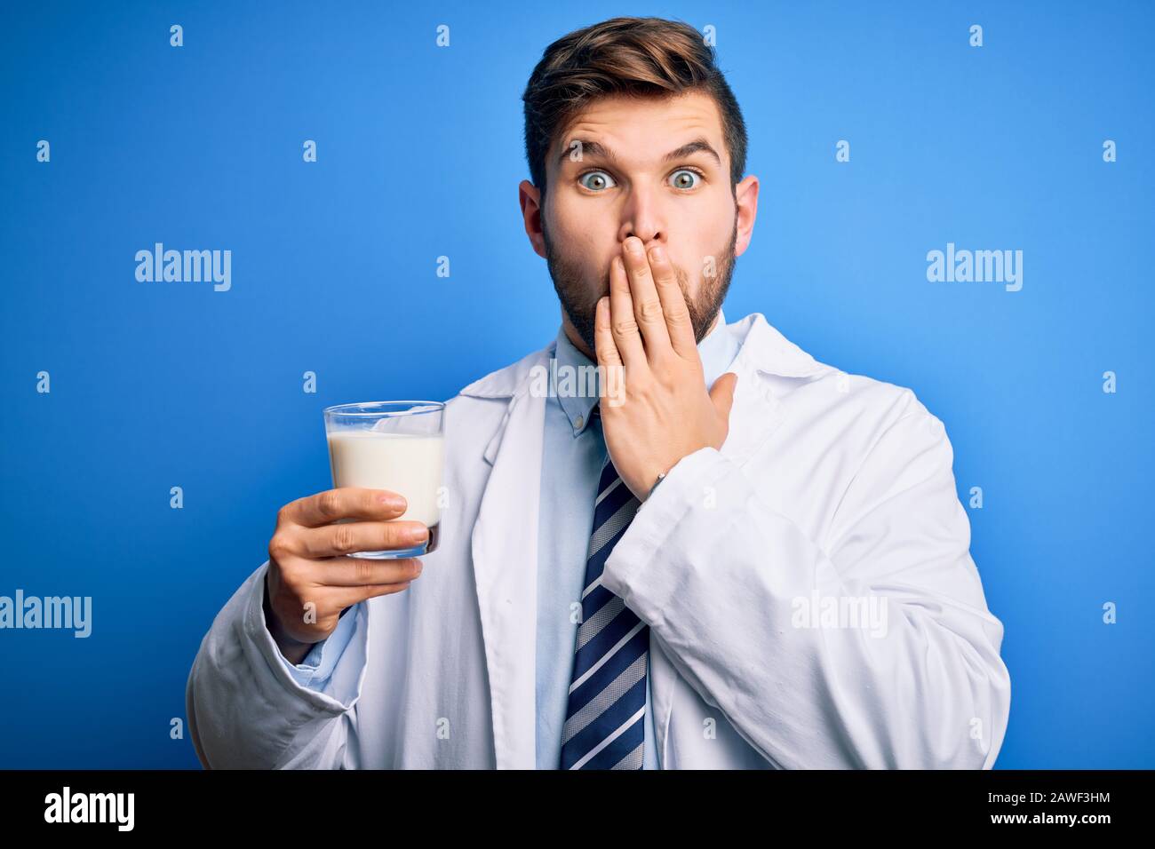 Young blond doctor man with beard and blue eyes wearing coat drinking ...
