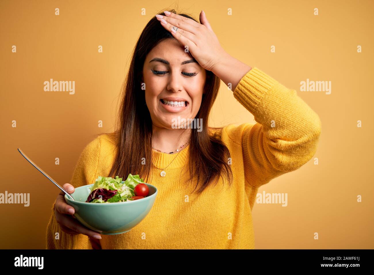Young beautiful woman eating healthy fresh salad over yellow background ...