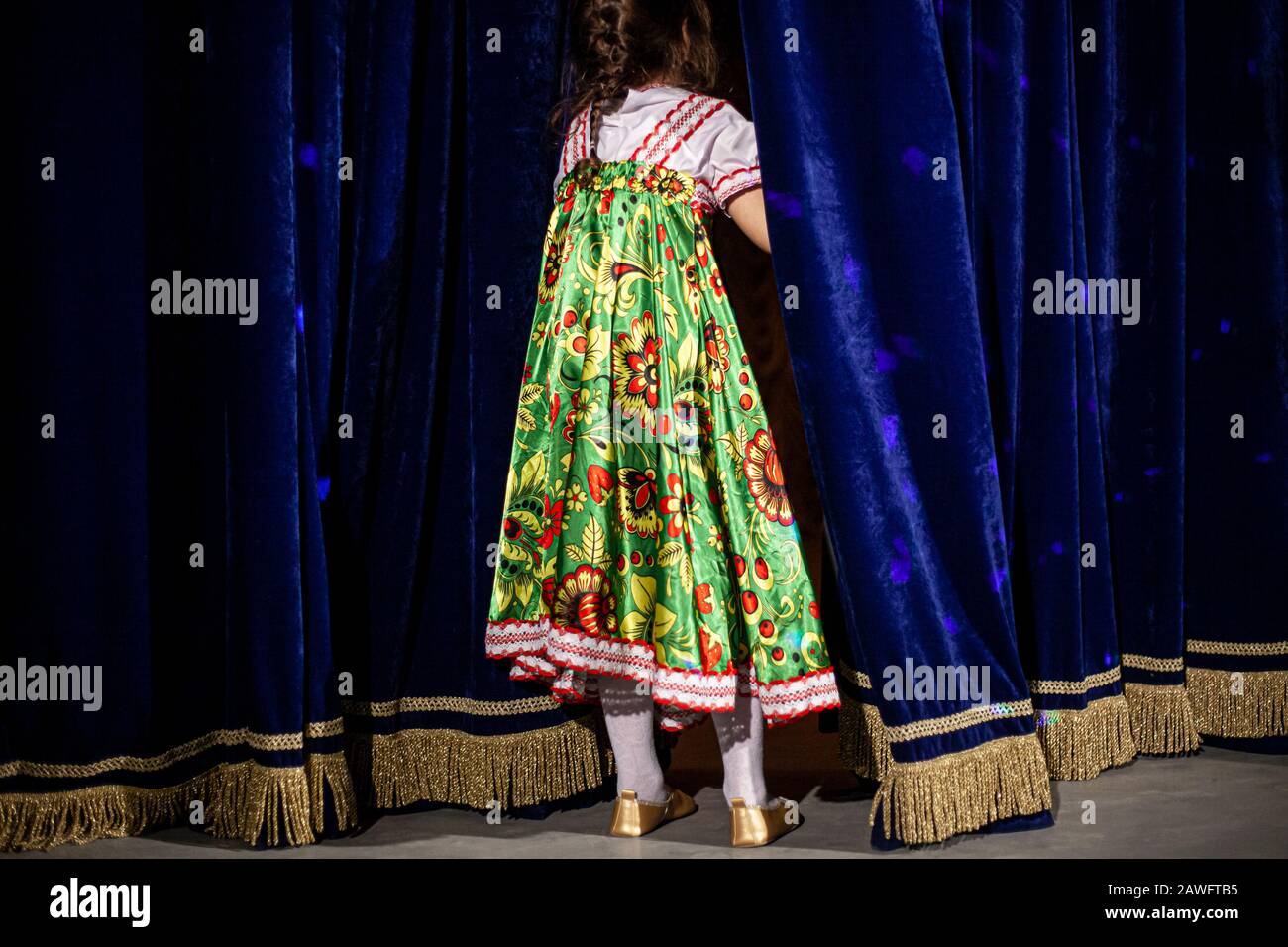 The child is waiting for a performance on stage. A girl peeks behind ...