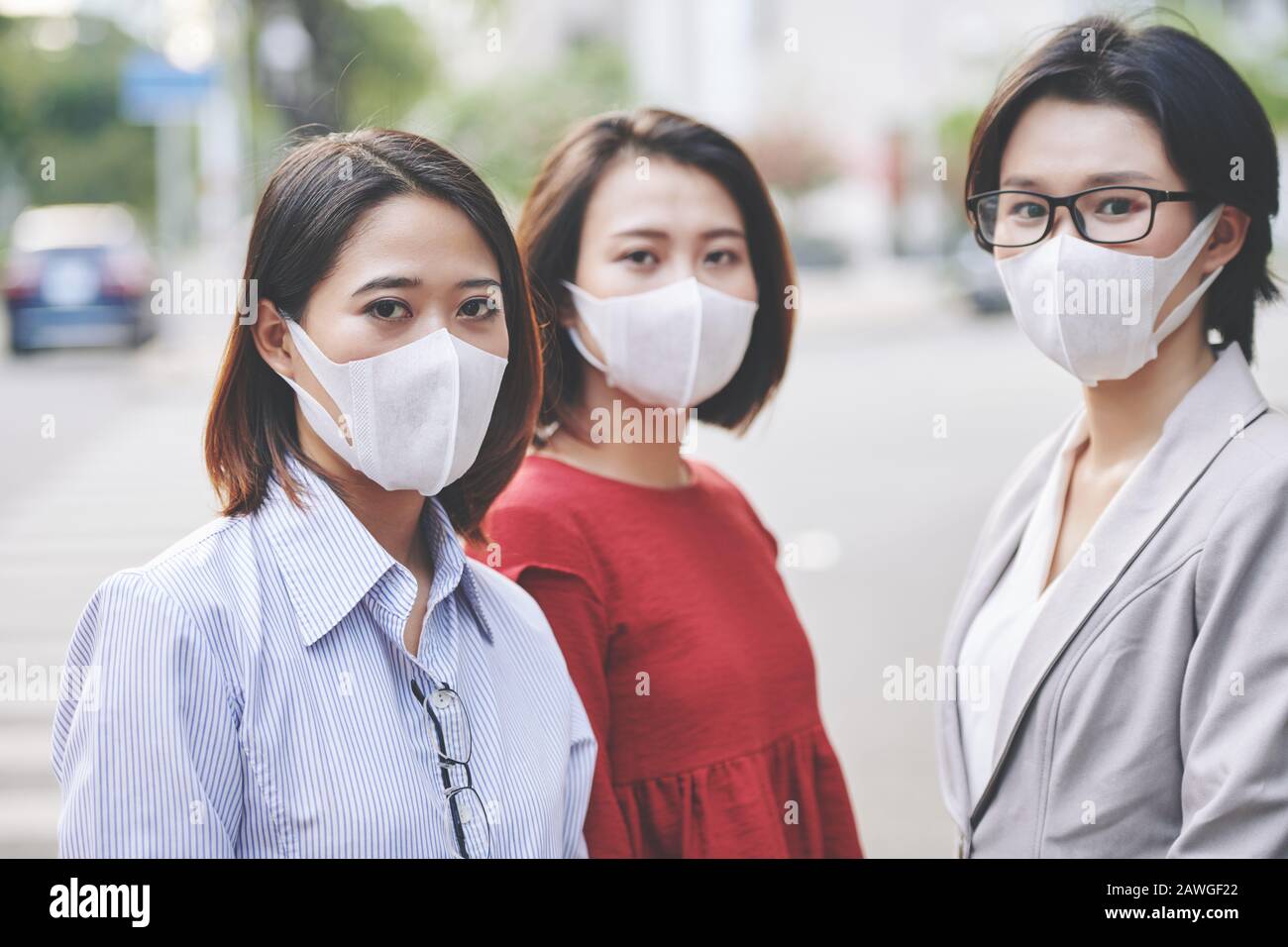 Group of serious young Asian women in antibacterial masks stranding in ...