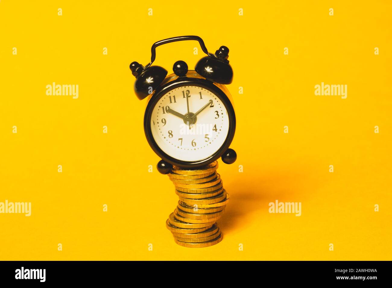 Time is money concept. classic alarm clock with coins on yellow ...