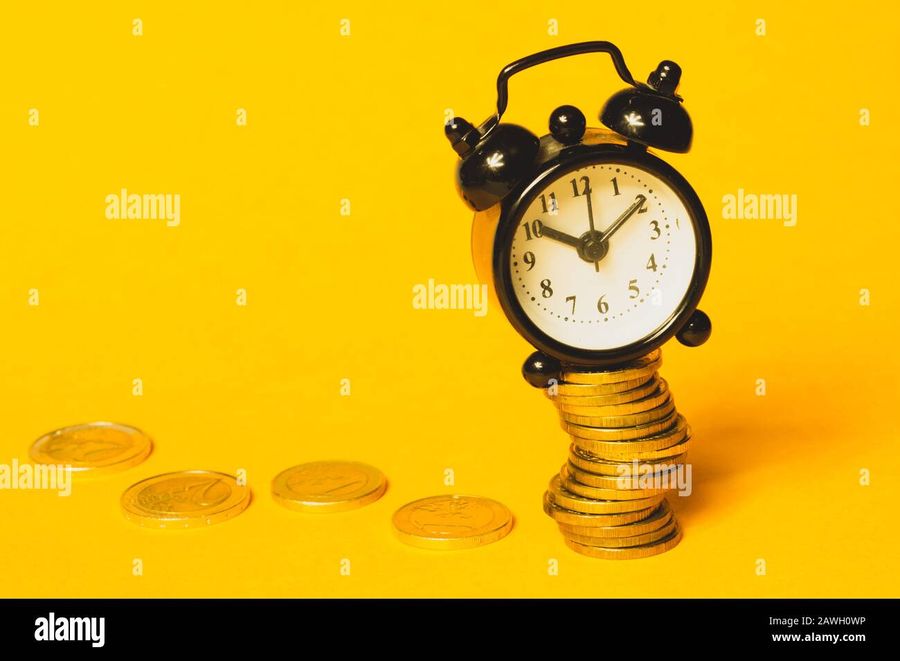 Time is money concept. classic alarm clock with coins on yellow ...