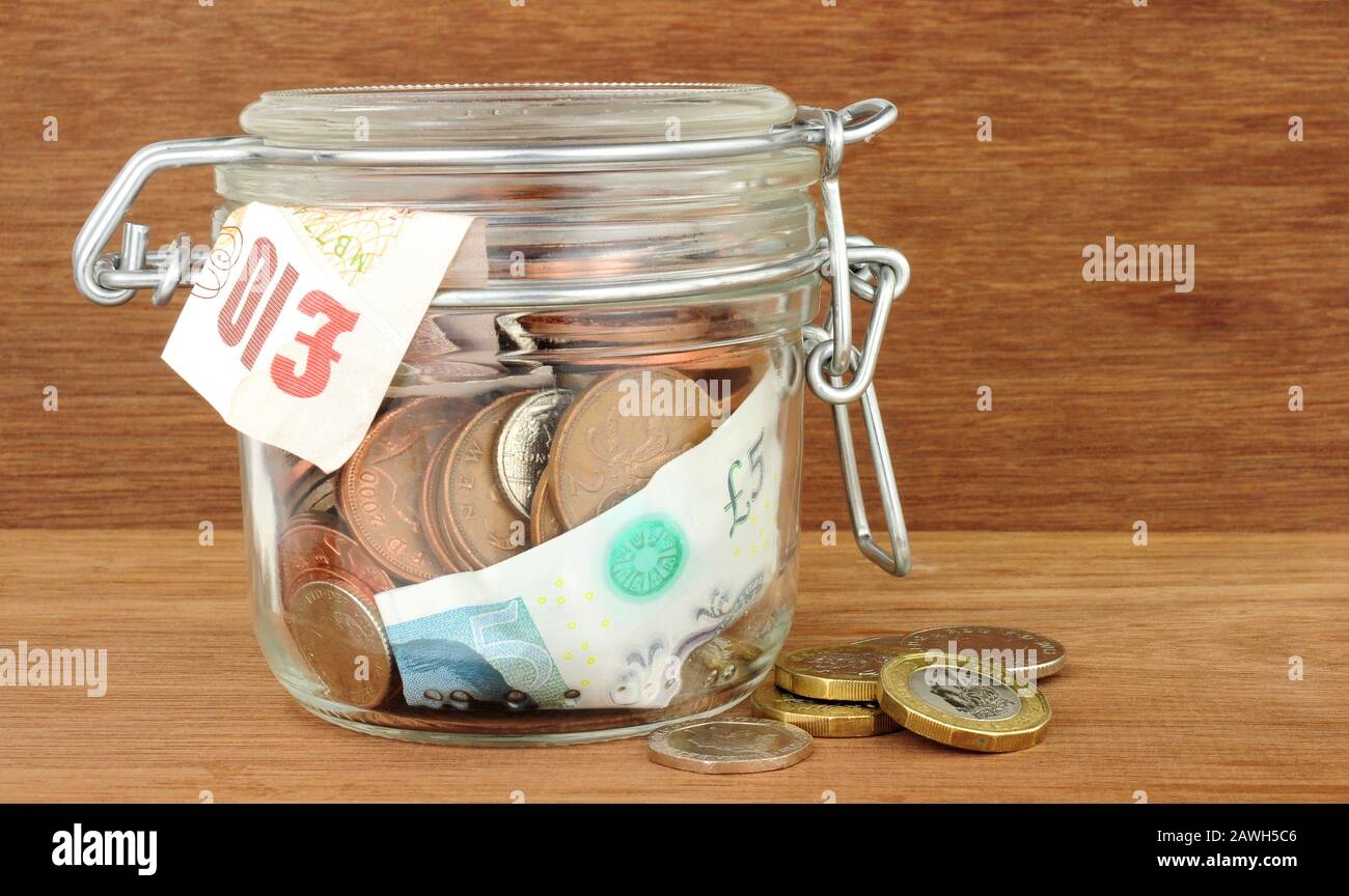 Glass jar filled with cash savings on a wood background Stock Photo - Alamy