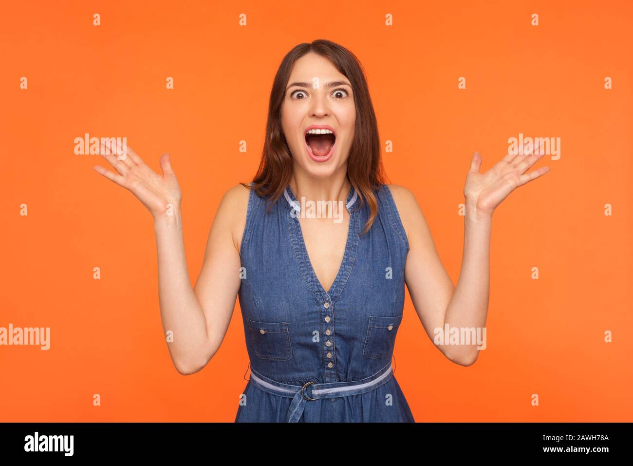 Shocked impressed brunette woman in denim outfit standing with wide ...