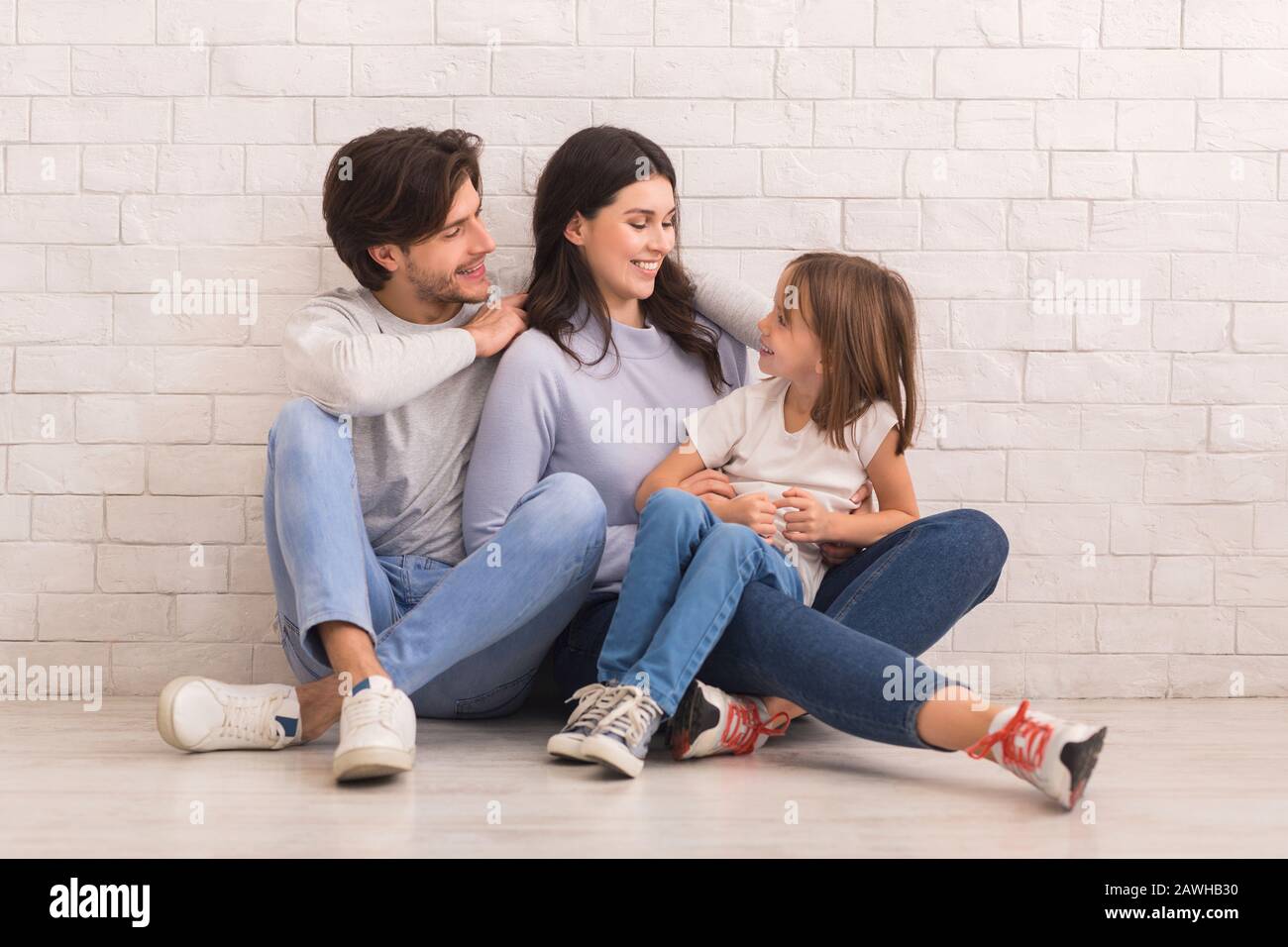 Affectionate Young Family Bonding Together While Sitting On Floor At ...