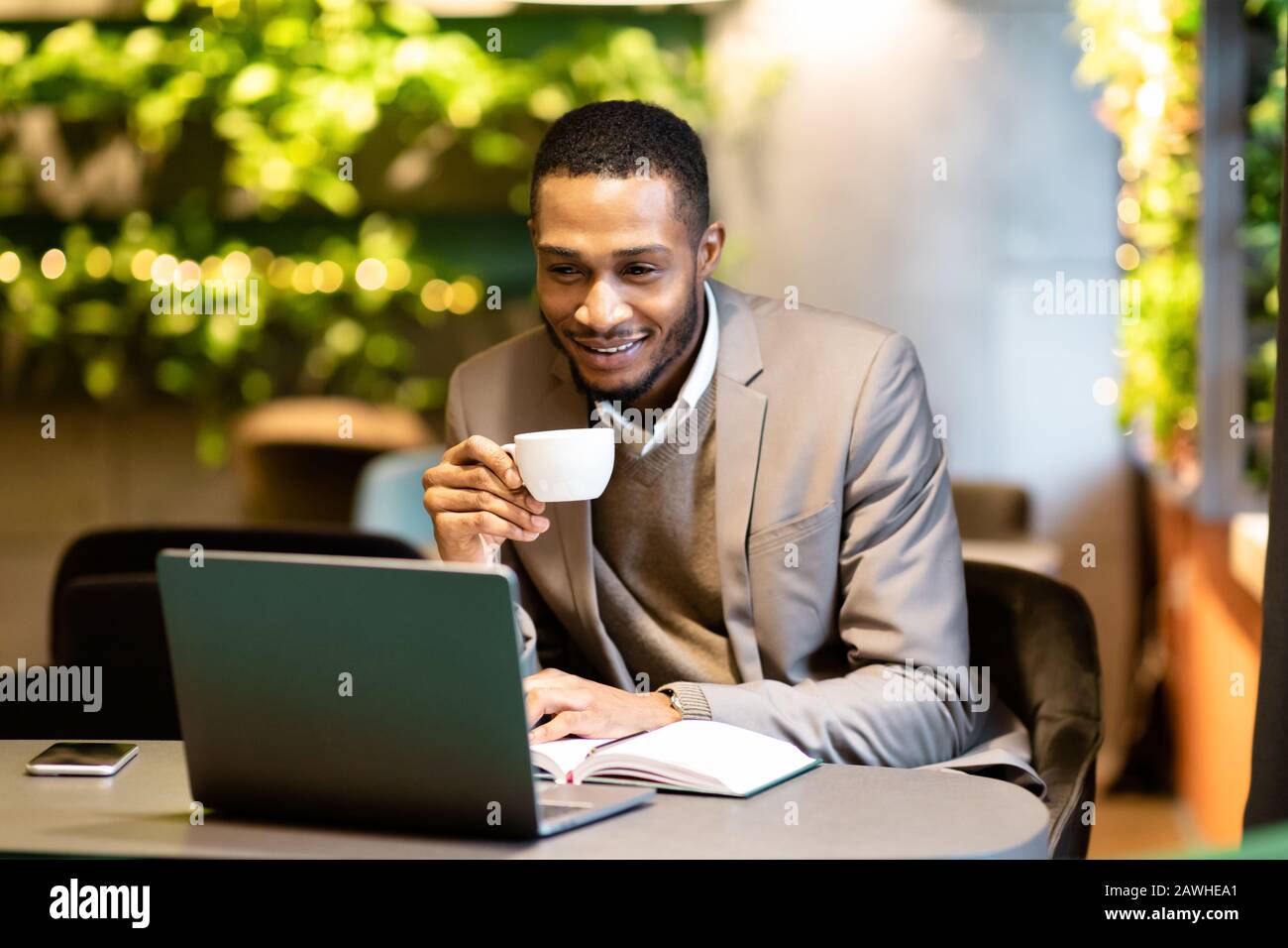 Afro guy drinking tea and using personal computer Stock Photo - Alamy