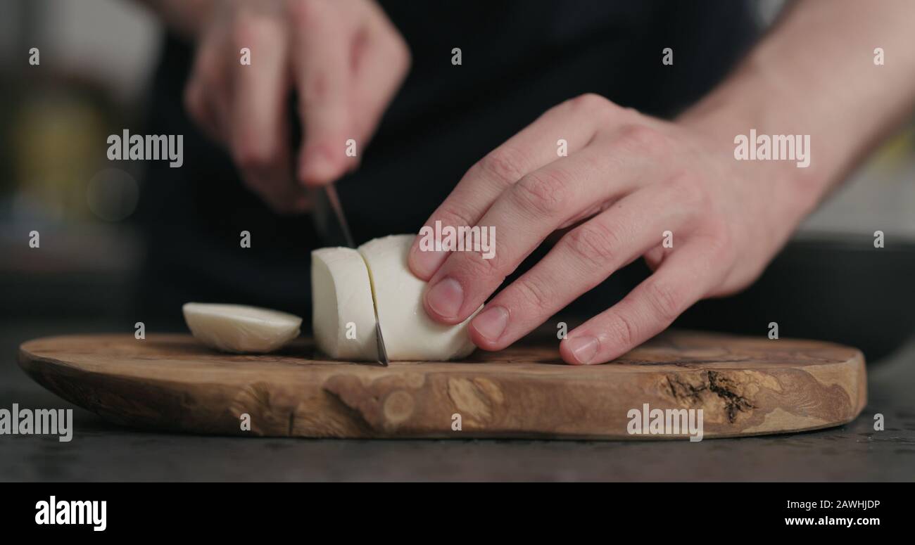 man slicing fresh mozzarella cheese on olive wood board, wide photo ...