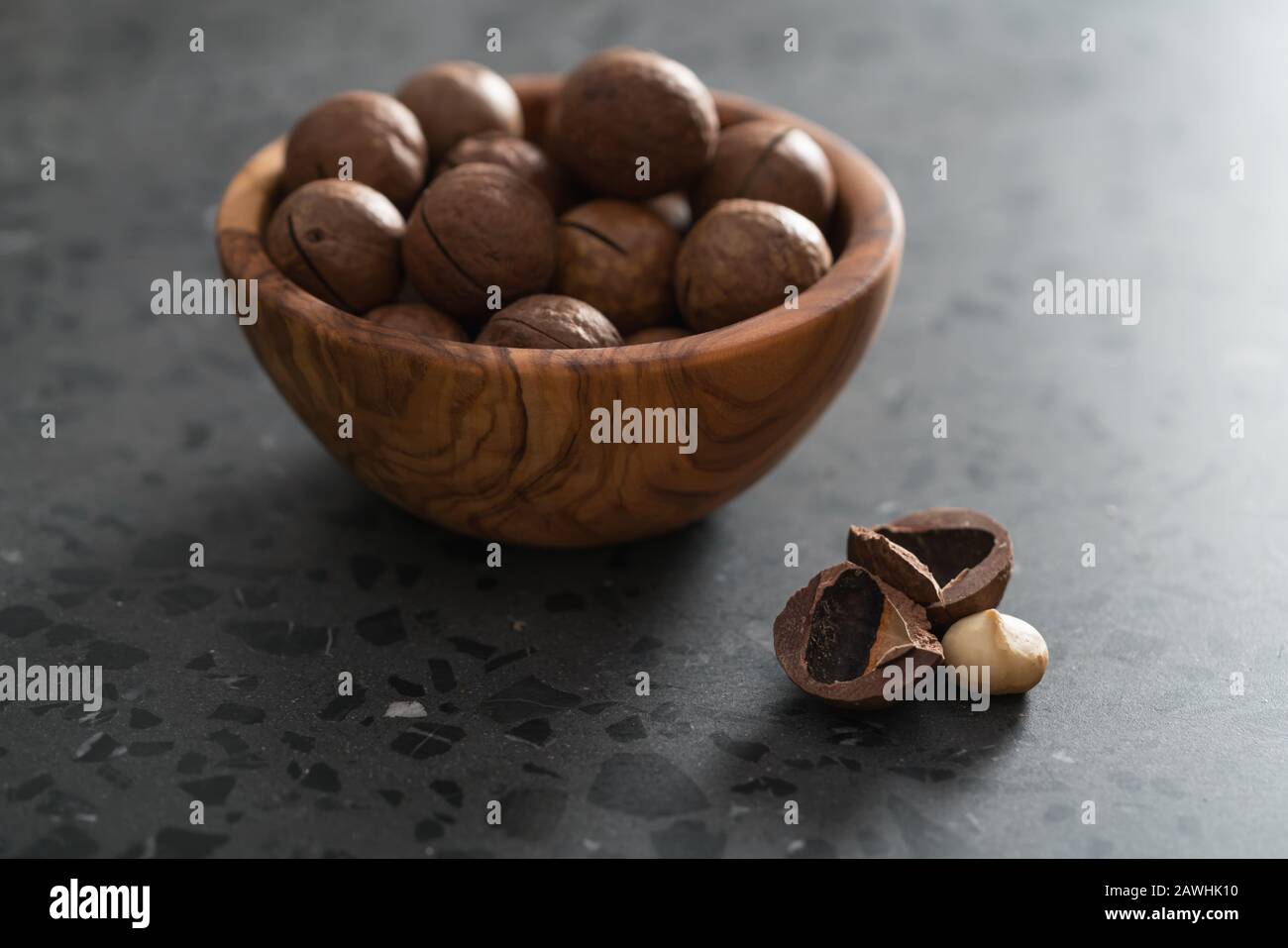 Inshell macadamia nuts in olive wood bowl on terrazzo surface, shallow ...