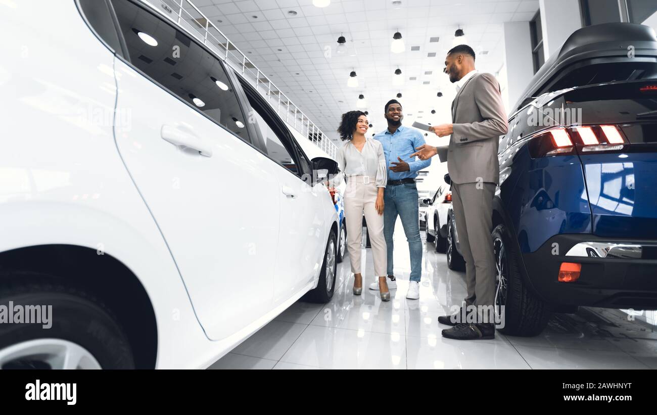 Afro Salesman Selling Car To Customers Standing In Dealership Showroom ...
