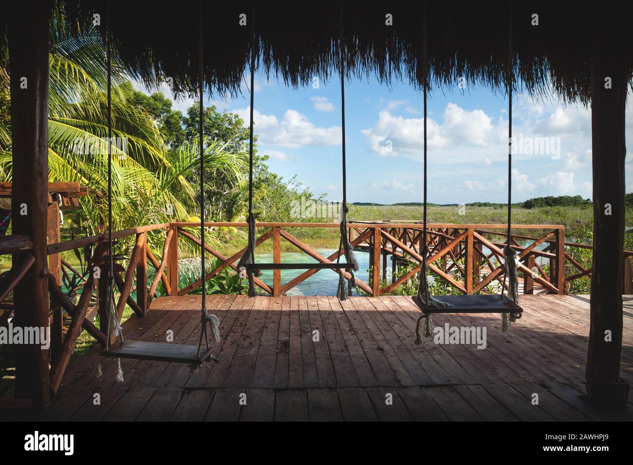 Swings on sunny pier along turquoise lagoon surrounded by tropical ...