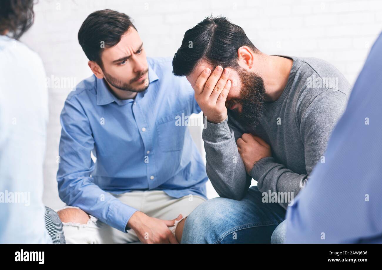 Group members comforting crying addicted man at rehab session Stock ...