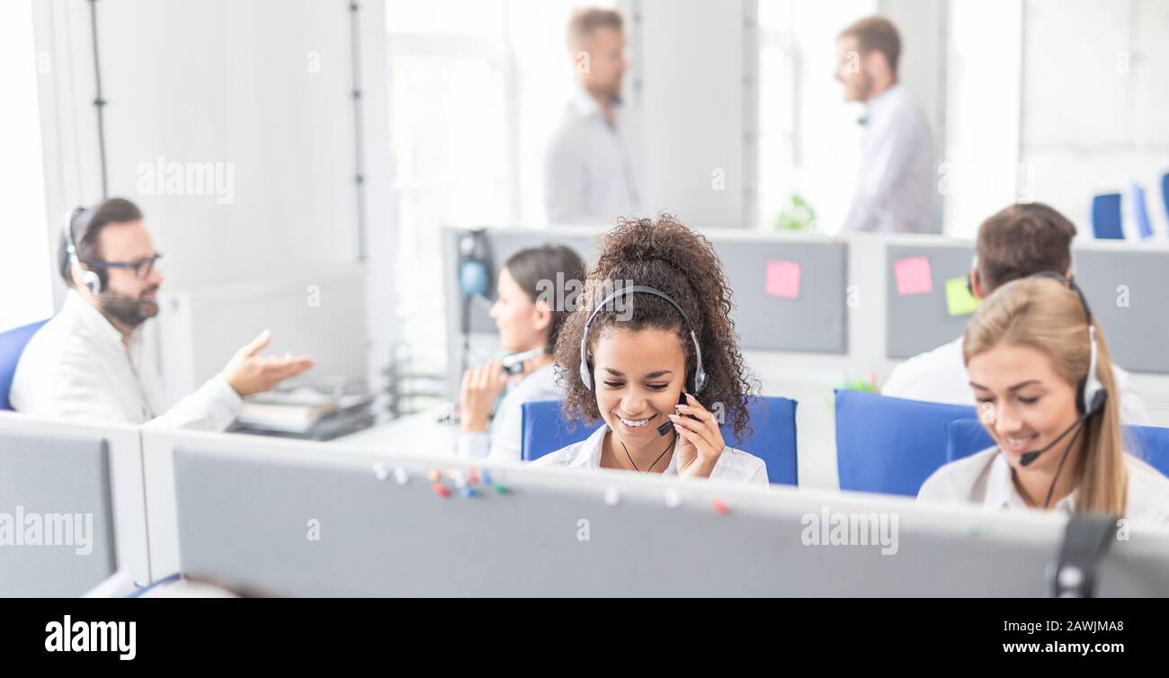 Call center worker accompanied by her team. Smiling customer support operator at work. Young ...