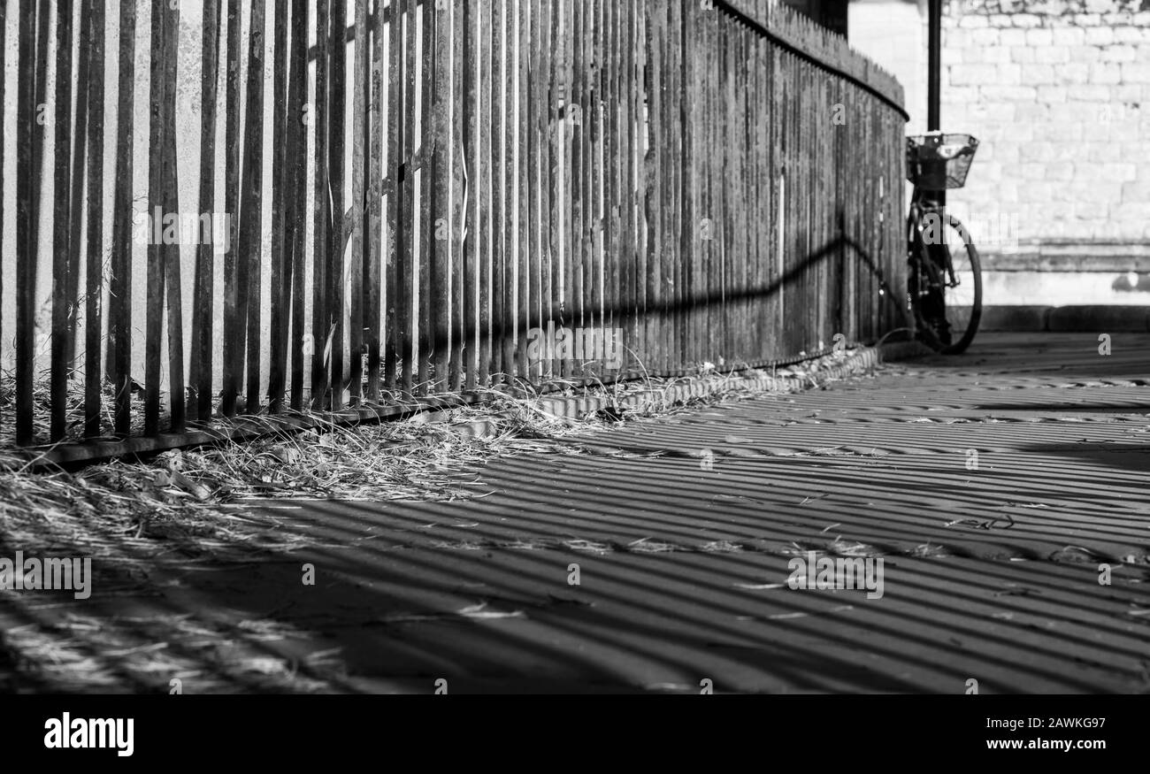 Close up of black painted railings and their shadows beside a pathway ...