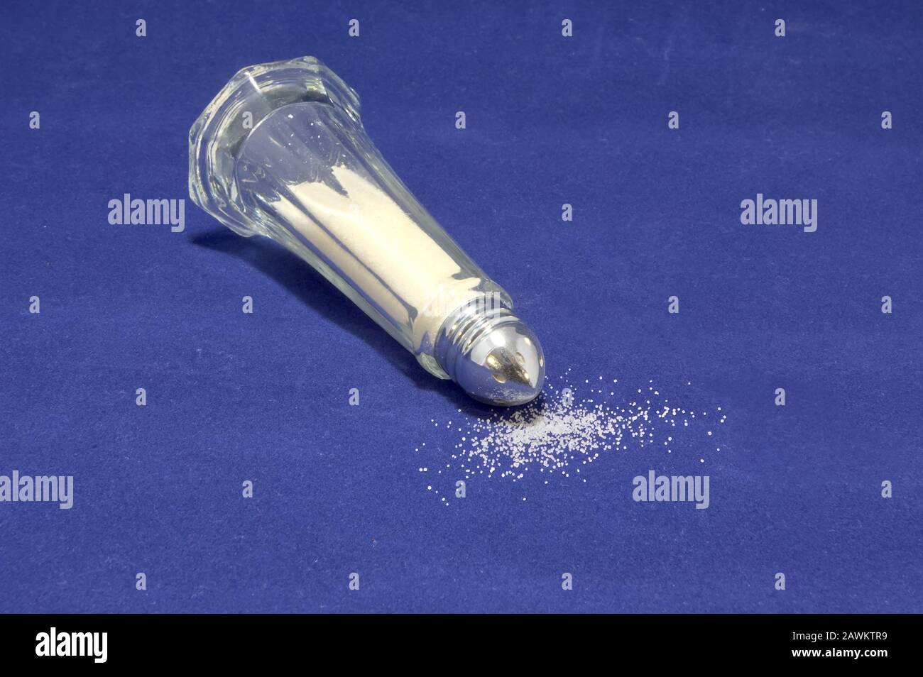 A Salt Shaker tipped over spilling some salt on blue velvet Stock Photo ...